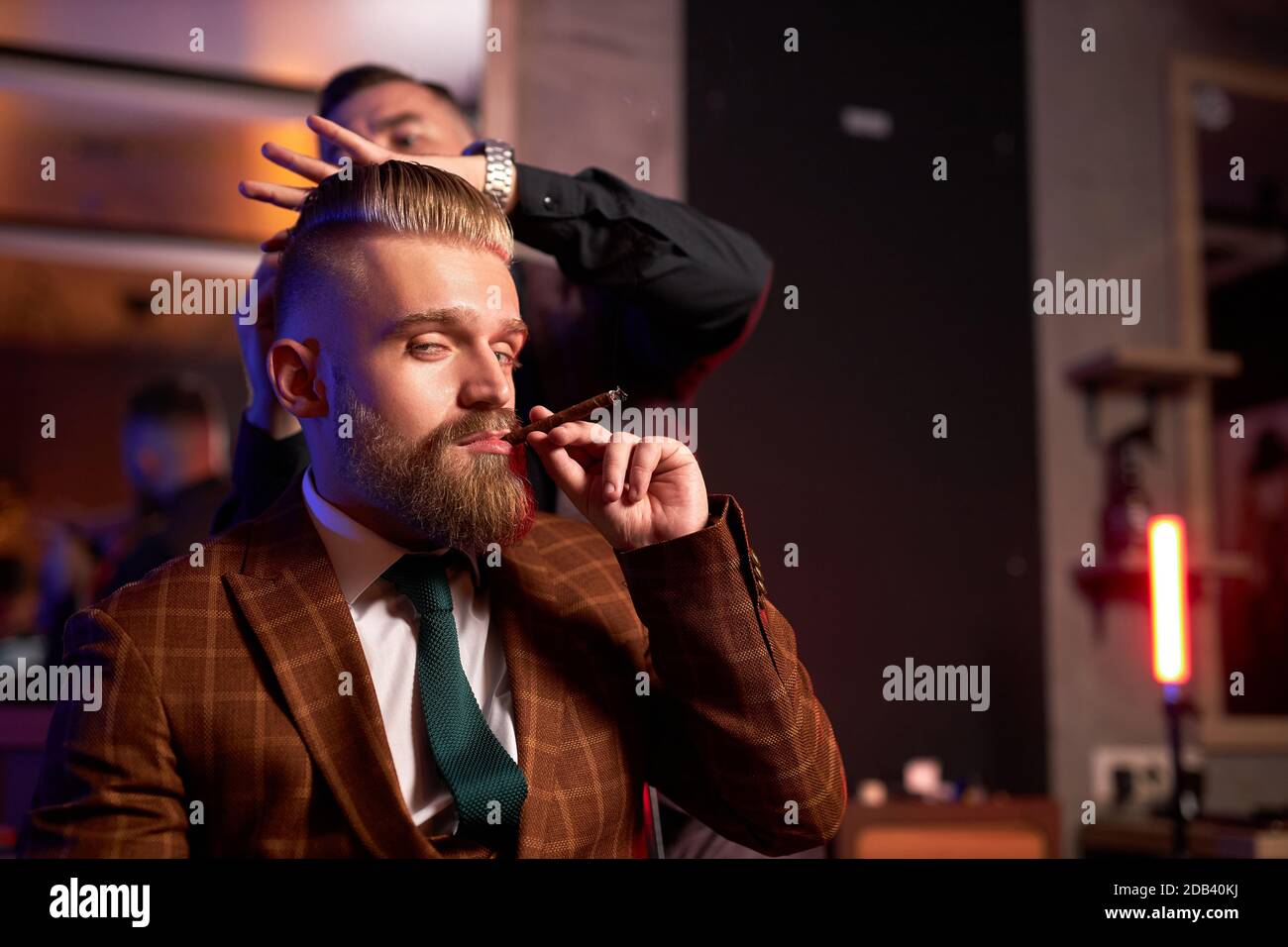 young caucasian barber cutting hair of his cool rich client sitting in ...