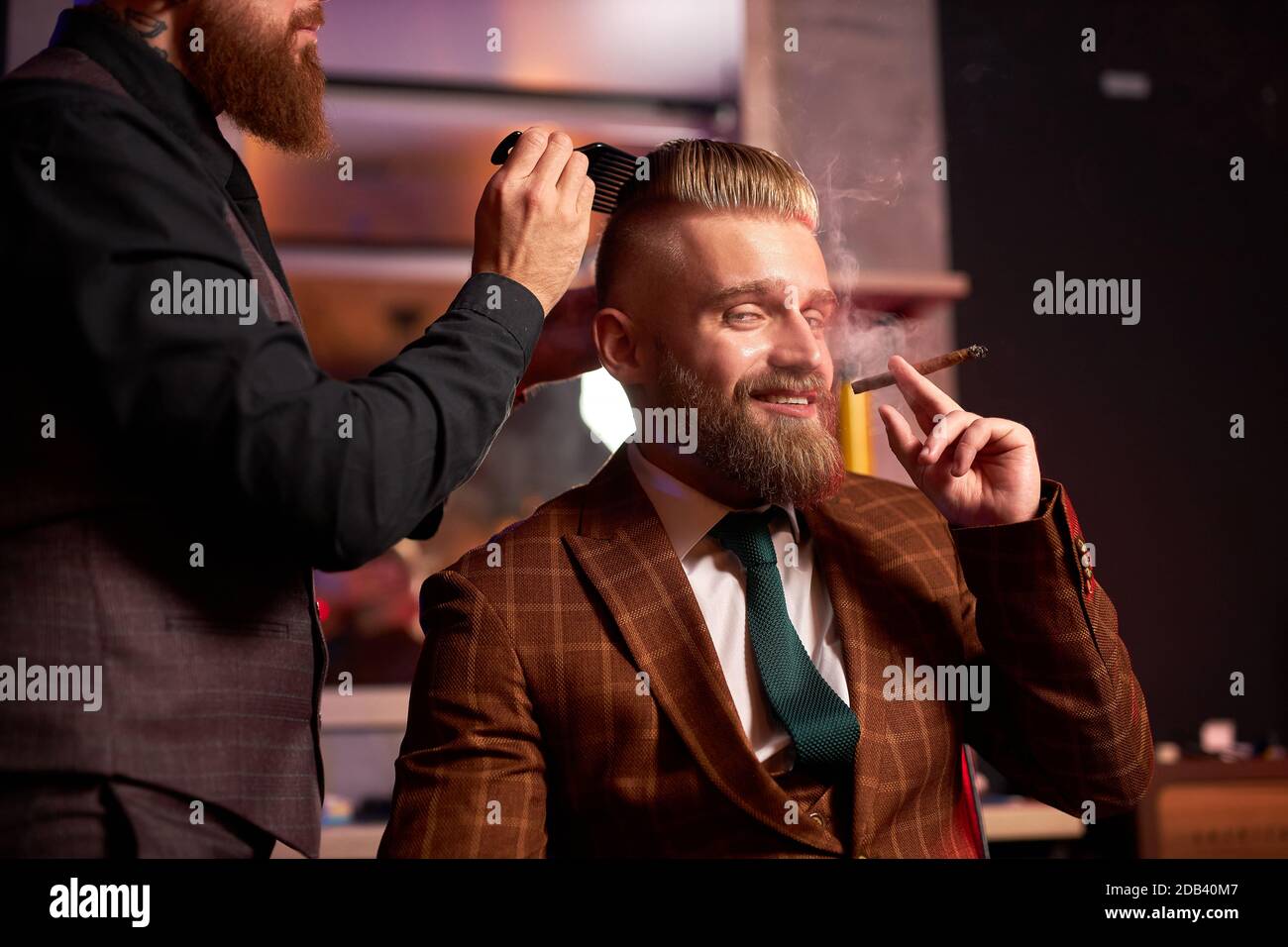 young caucasian barber cutting hair of his cool rich client sitting in ...
