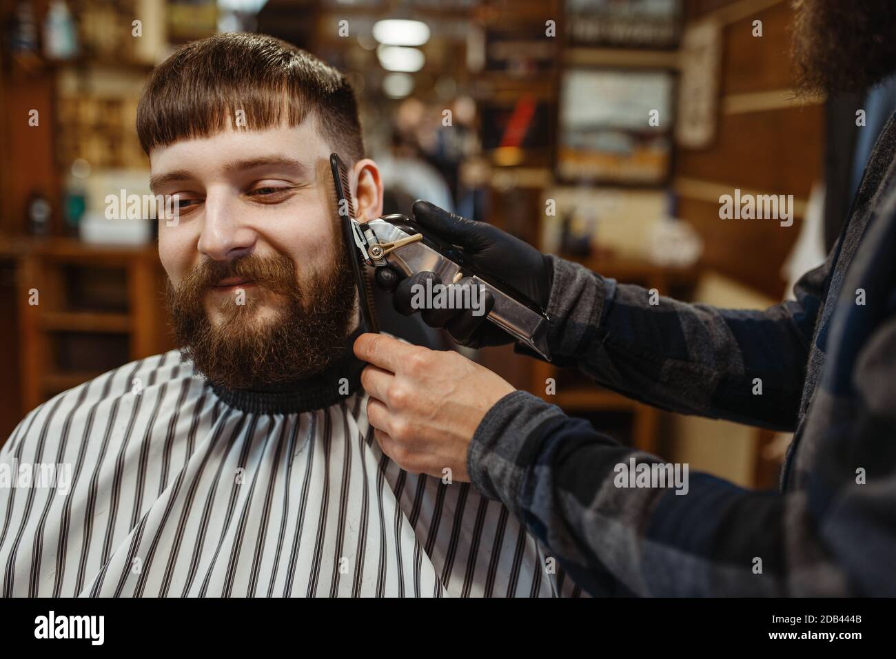 Barber with comb and electric clipper makes a haircut to a client ...
