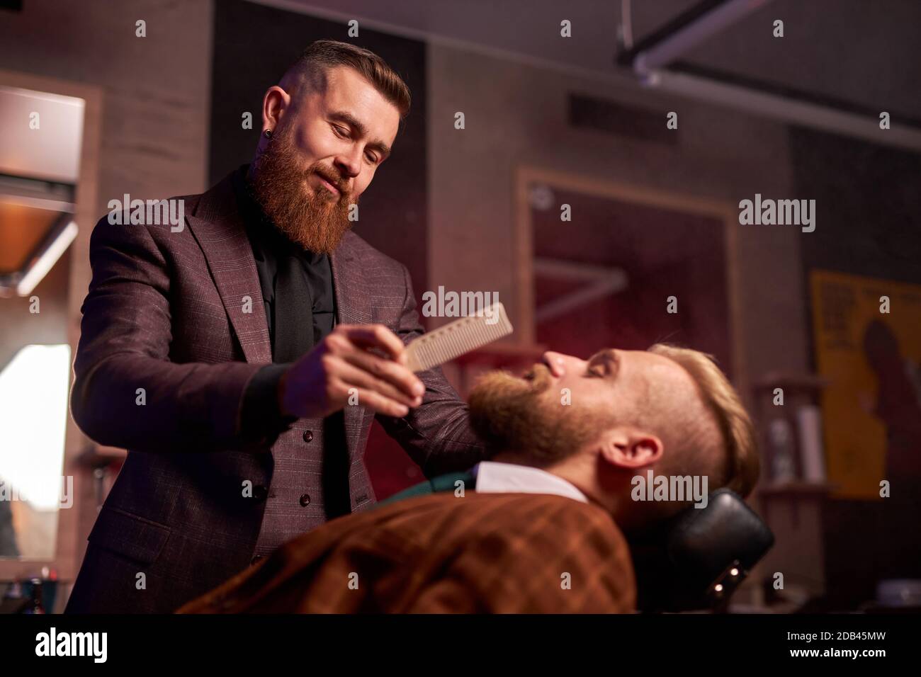 hairstyling process. barber cutting beard of caucasian male with the ...