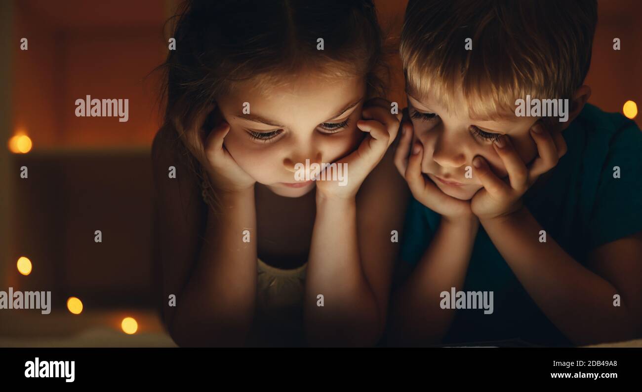 Portrait of little kids at night watching cartoons on the tablet, sad ...