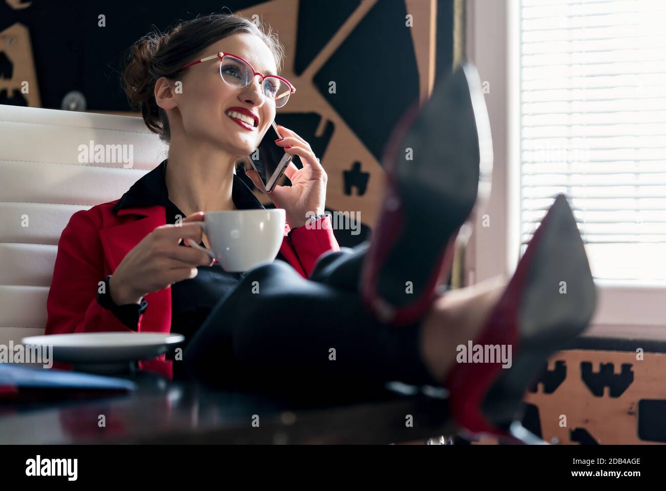 Businesswoman having a coffee using the phone putting feed on desk in ...