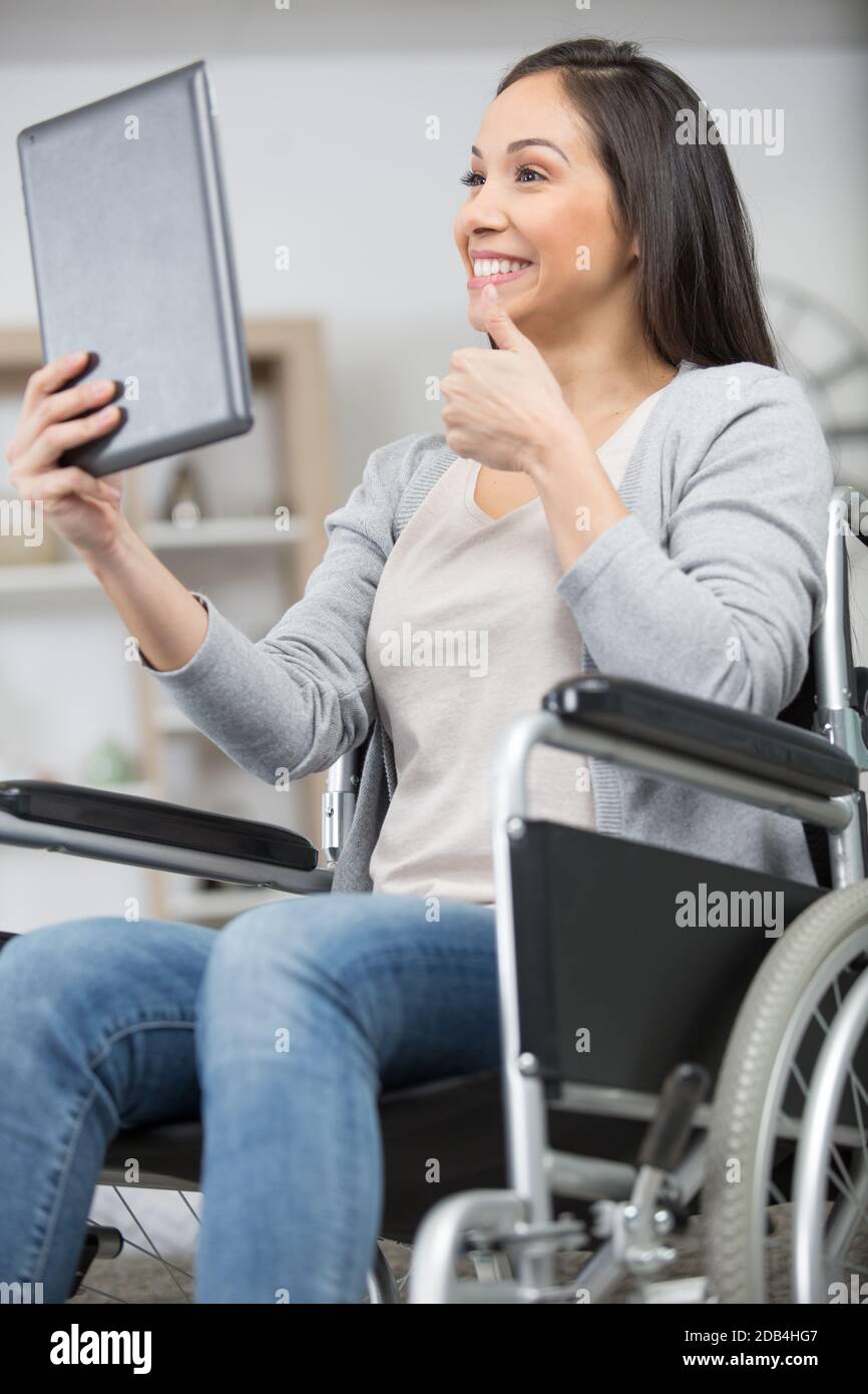 disabled woman making thumbs-up gesture during live chat on tablet ...