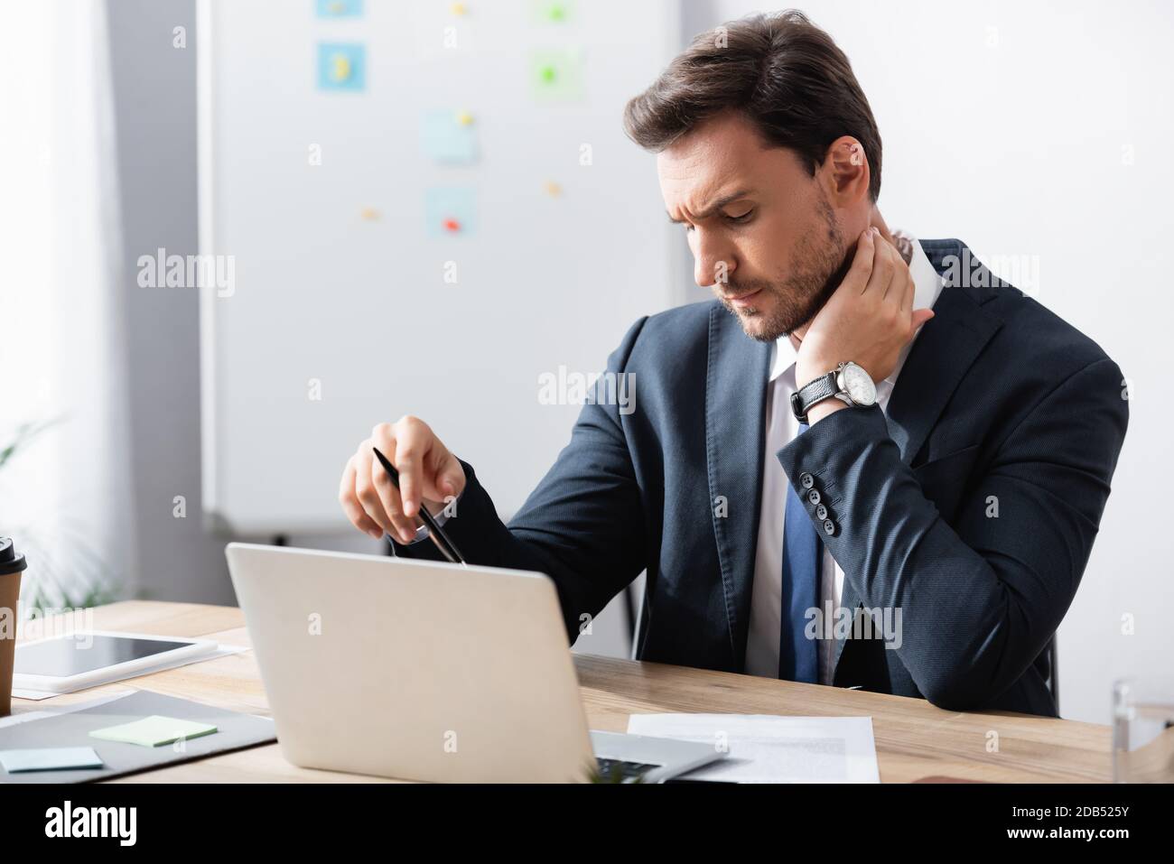 Businessman with painful neck sitting at workplace on blurred ...