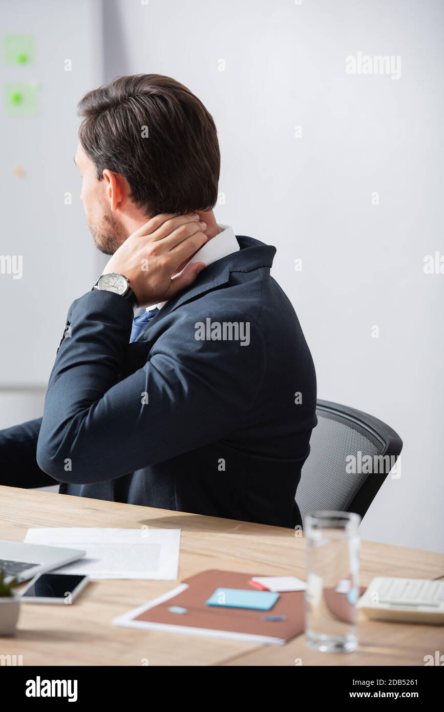 Office worker with painful neck sitting at workplace on blurred ...