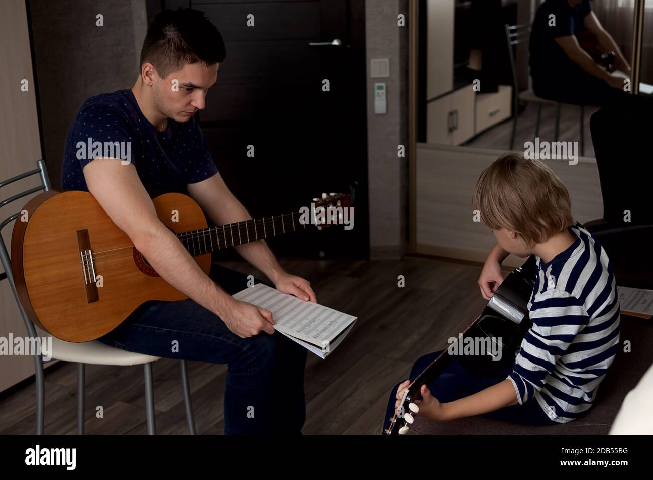 Young male musician teaches little boy student how to play the acoustic ...