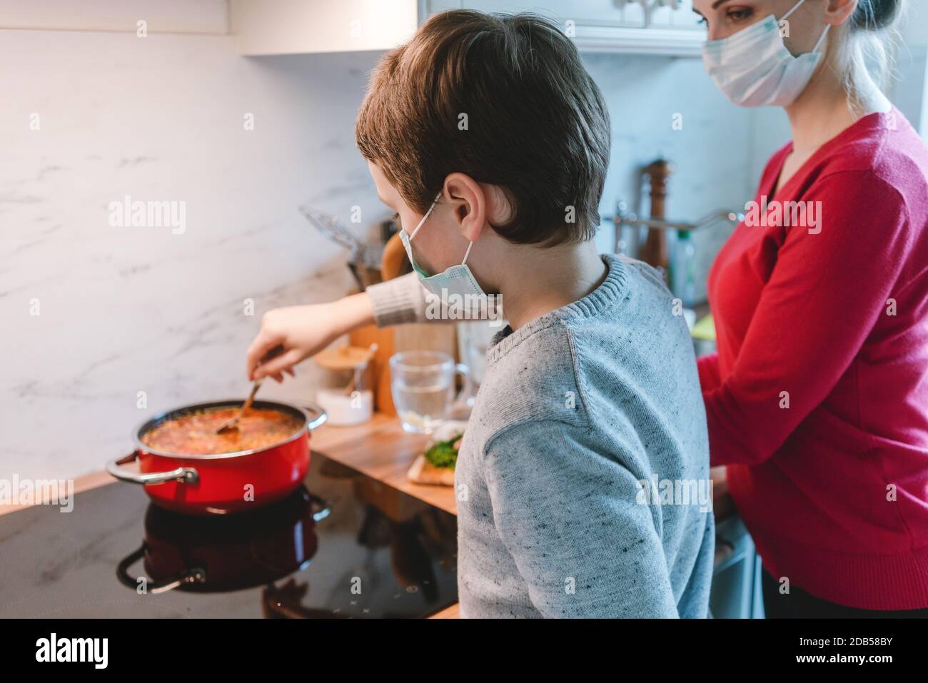 Mother and son cooking at home together wearing masks in the kitchen ...
