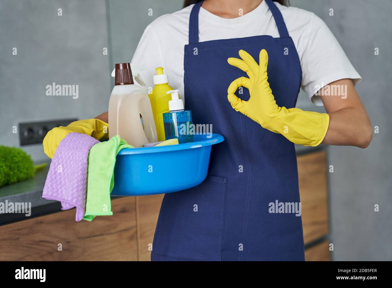 Cropped shot of cleaning lady showing ok sign while holding container ...