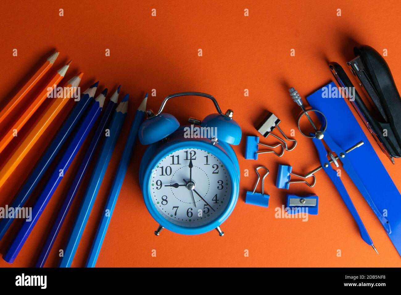 Pencils, blue alarm clock, compass, ruler and stapler on an orange ...