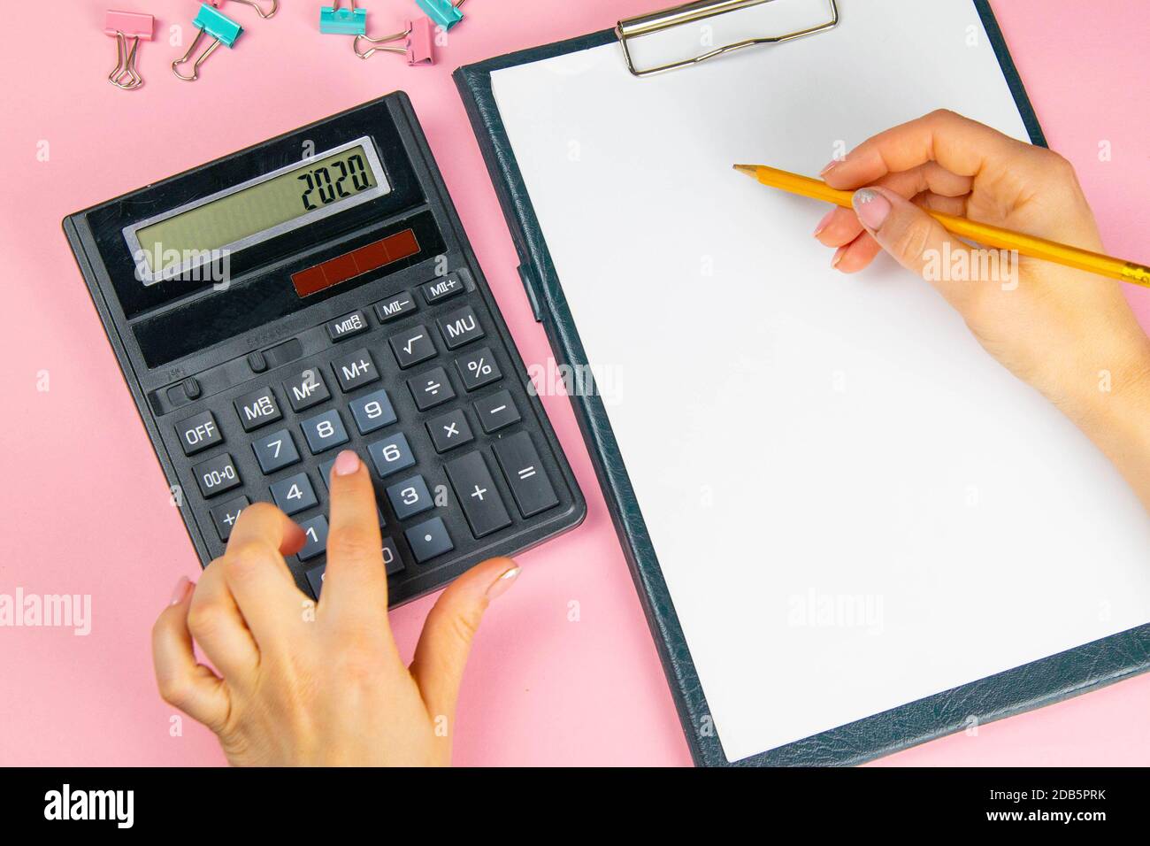 The hands of a woman count on a calculator and write notes. Top view of ...