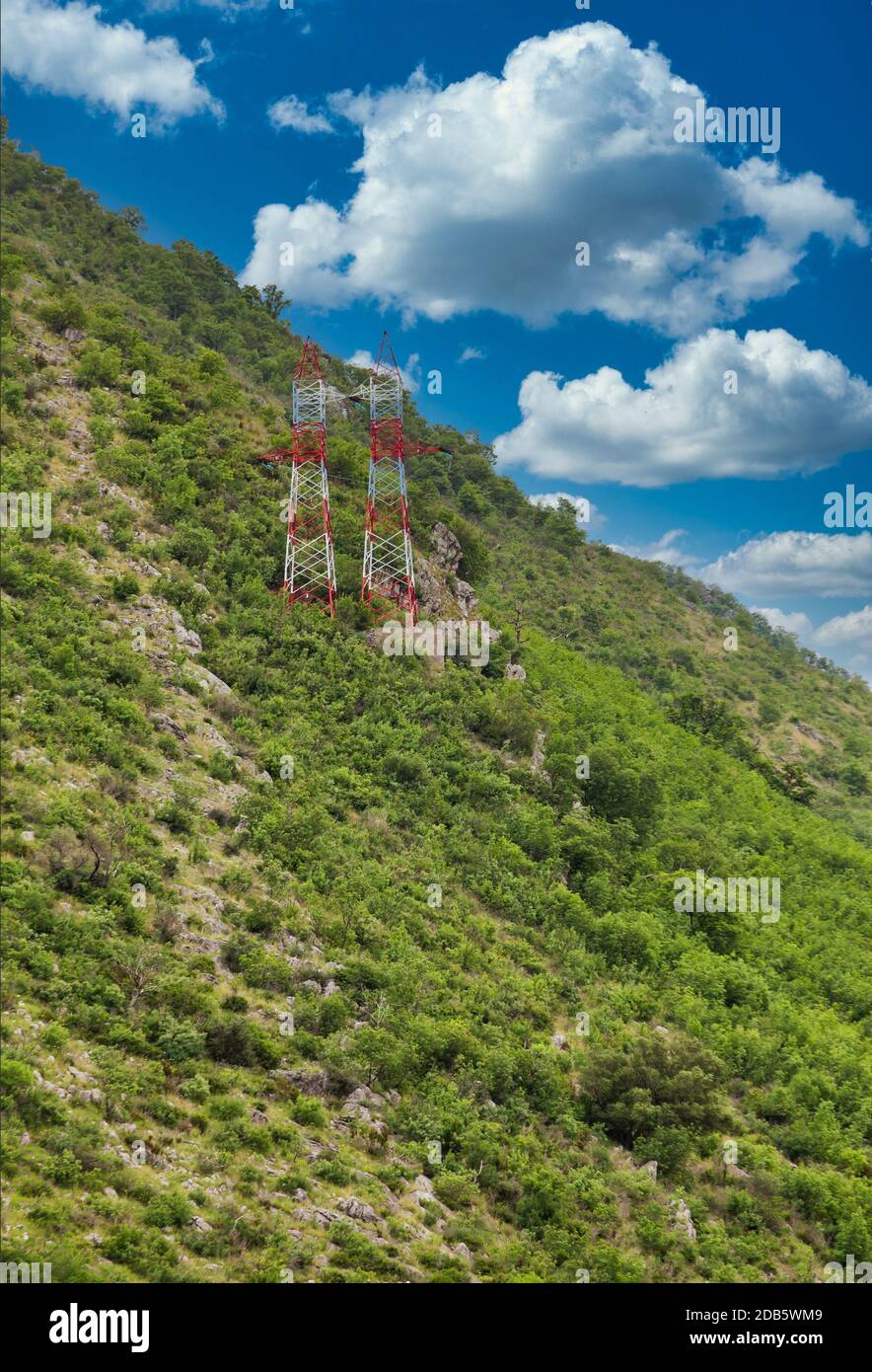 Red and white high power pylons on a steep green hill Stock Photo - Alamy