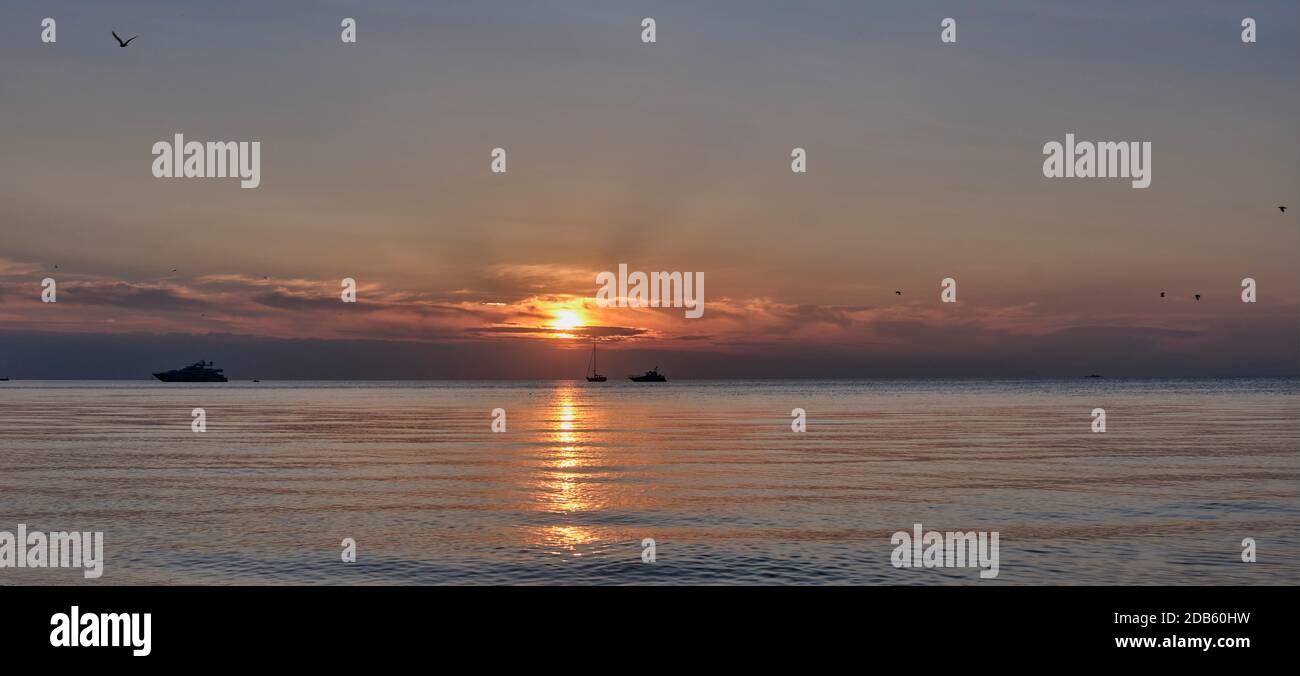 Bright colorful sunset over the sea with silhouettes of ships as ...