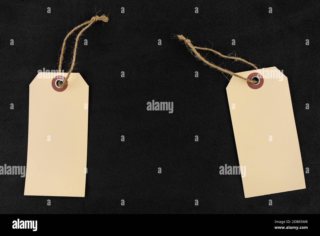 Two blank brown gift tags with a string lying on a black background ...