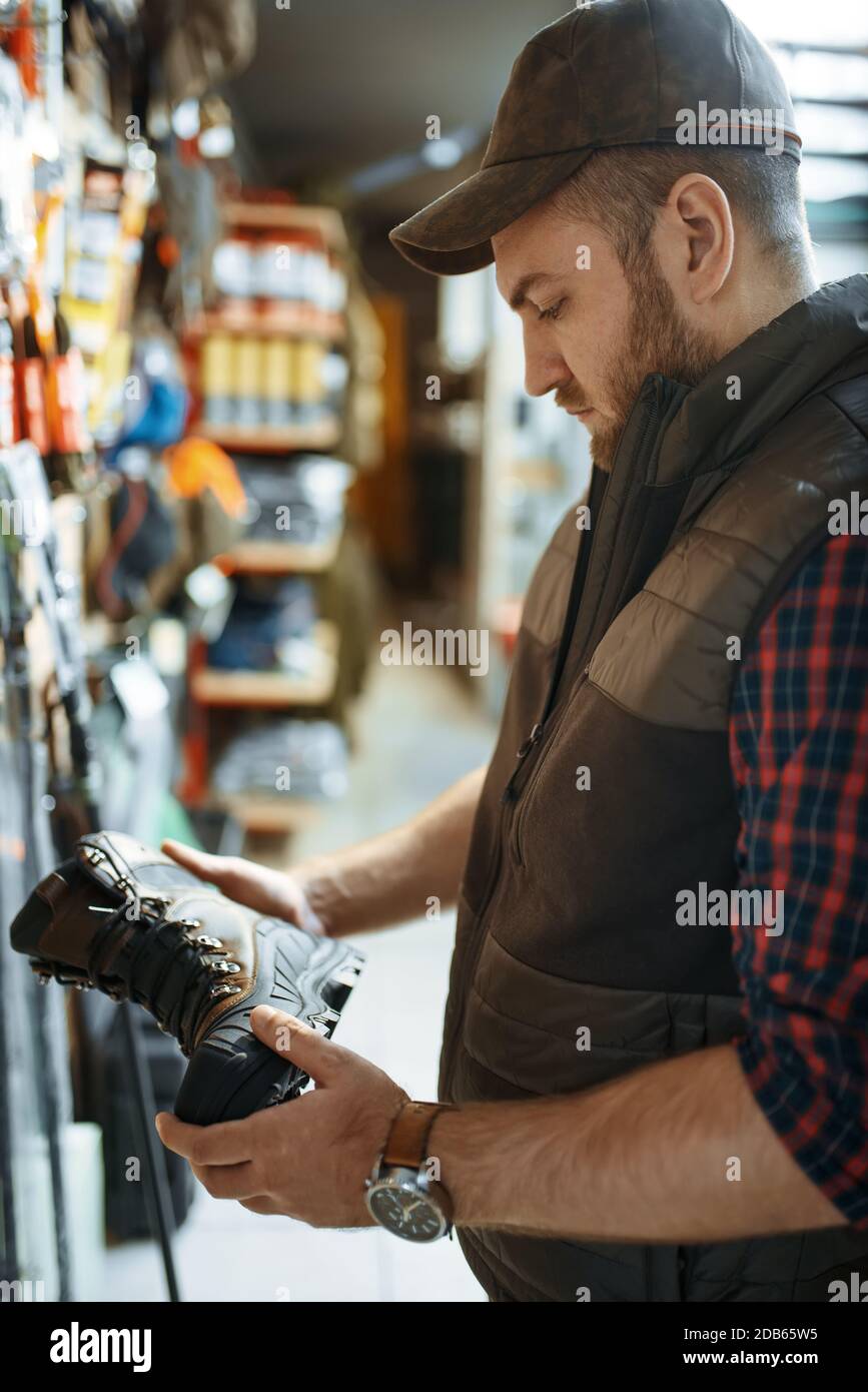 Man choosing boots for hunters at showcase in gun shop. Euqipment and ...