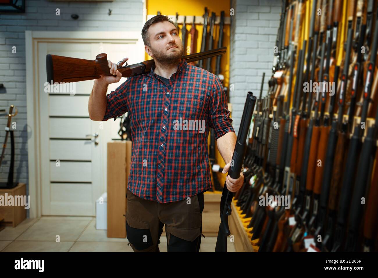 Man poses with two rifles at showcase in gun shop. Euqipment for ...