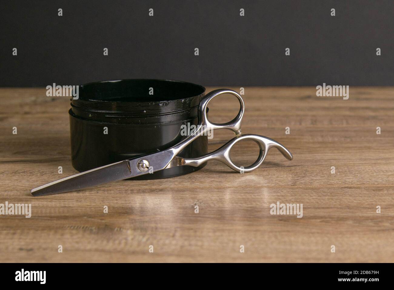 Scissors and a gel for haircuts stand on a wooden table at a black wall ...