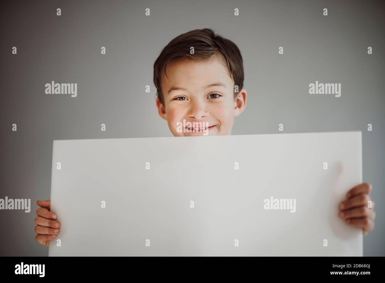 cool young boy holding white sign in front of grey background during ...