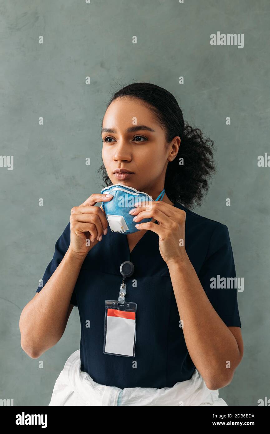 Portrait of female medical worker wearing a respirator at wall and ...