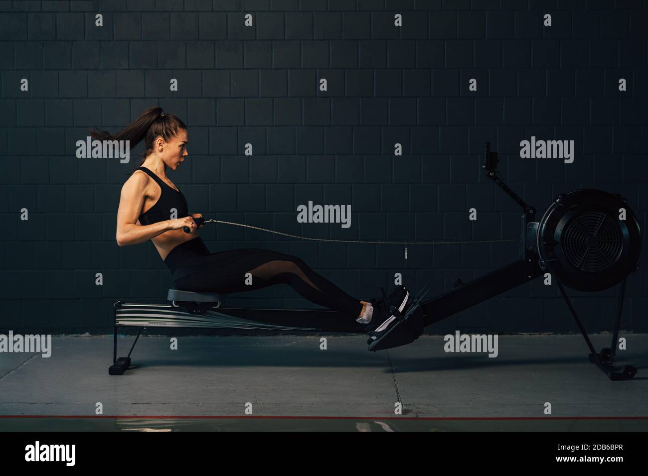 Side view of young muscular woman exercising in gym with rowing machine ...