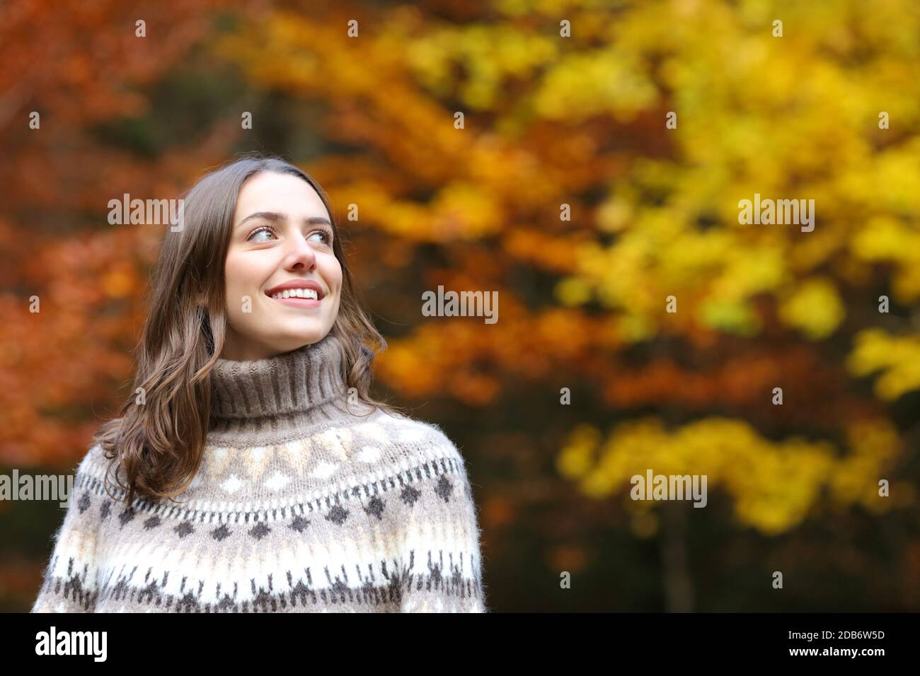 Happy woman looks at side contemplating standing in a park in autumn ...