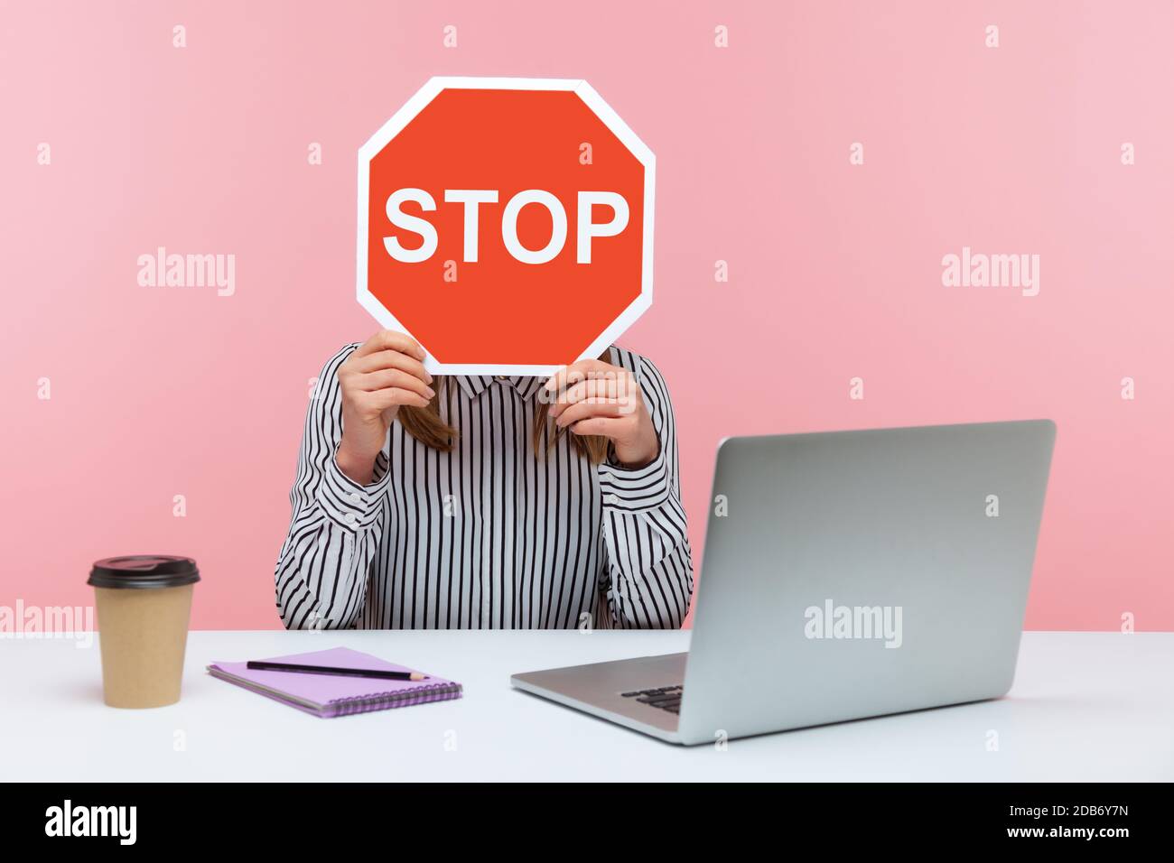 Female office worker in striped shirt sitting at workplace hiding face ...