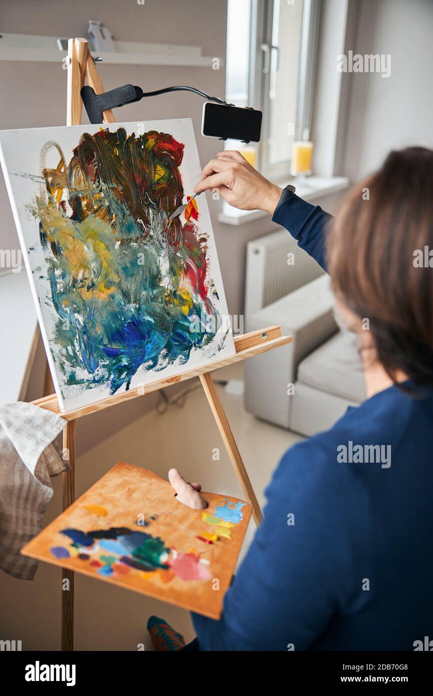 Focused artist putting more paint on his canvas Stock Photo - Alamy