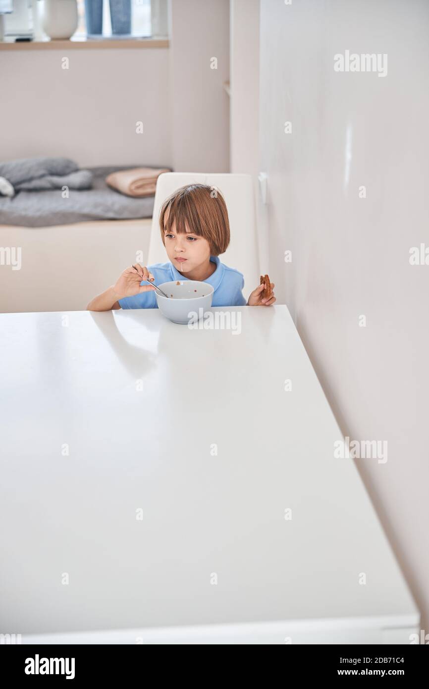 Cute kid sitting at kitchen table while having a meal Stock Photo - Alamy