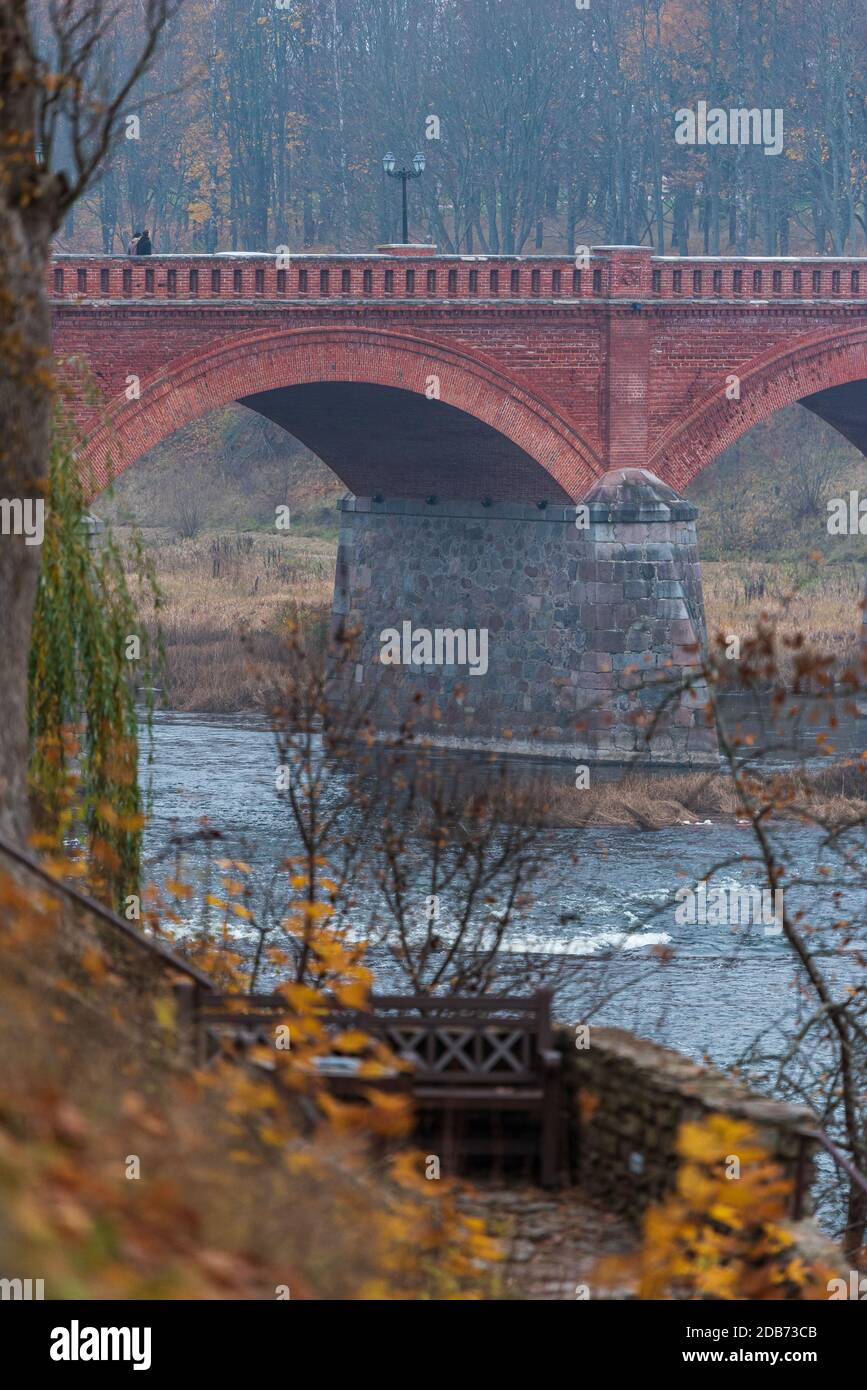 an old brick bridge in the fall and a river flowing under the bridge to ...