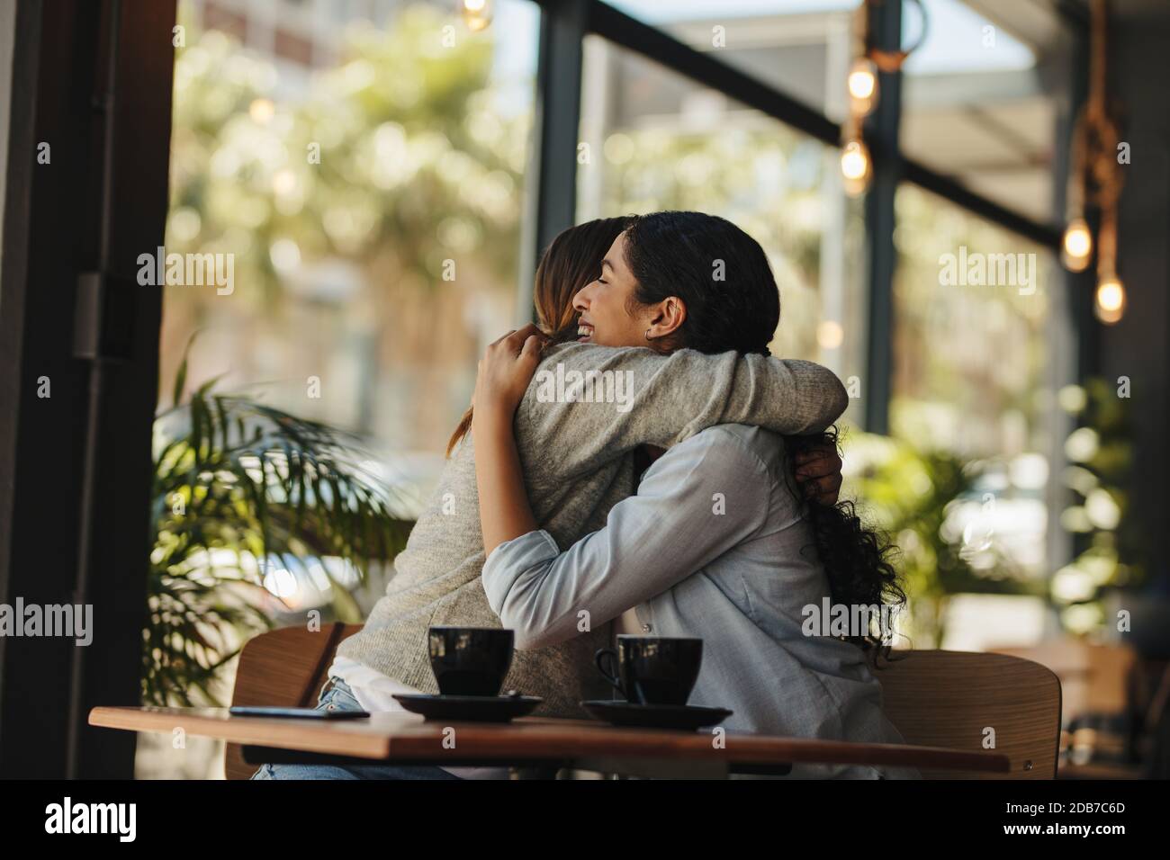 Woman greeting a friend at cafe. Female friends hugging each other at a ...