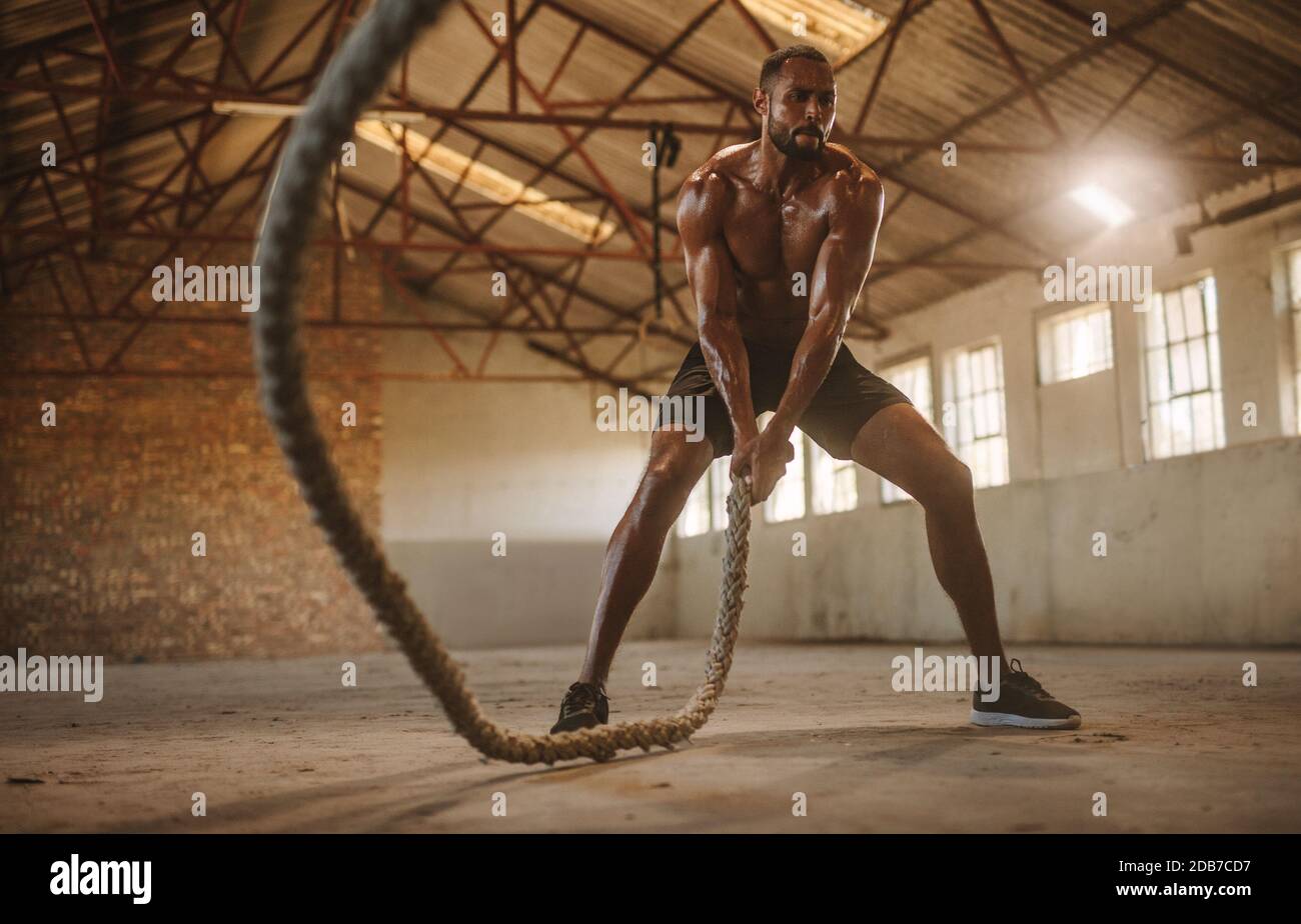 Strong and masculine man using training ropes for exercise at gym ...