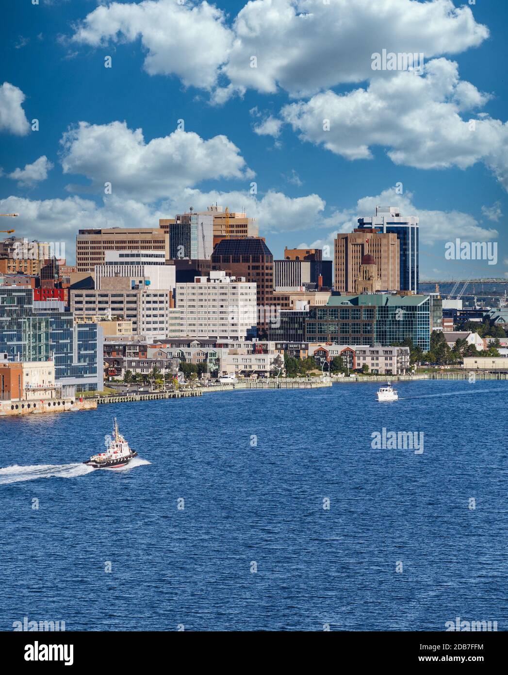 A tugboat sailing past the city of Halifax, Nova Scotia in blue water ...
