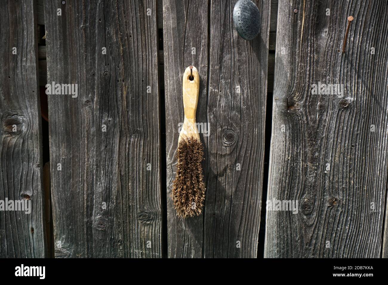 A closeup of a brush with a wooden handle hanging on the wooden fence ...