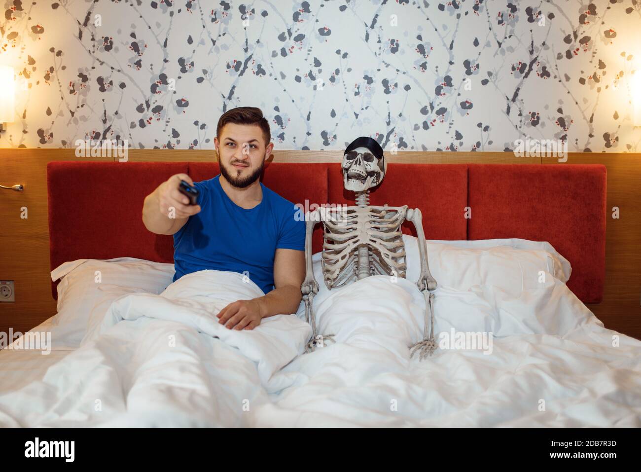 Man and human skeleton watching TV in the bed, bad relationship. Couple ...