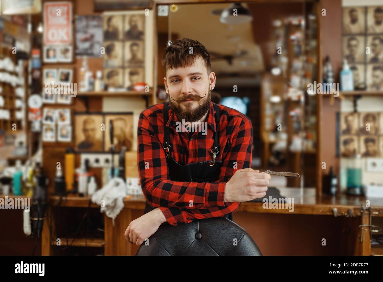 Barber with razor blade poses at the chair. Professional barbershop is ...