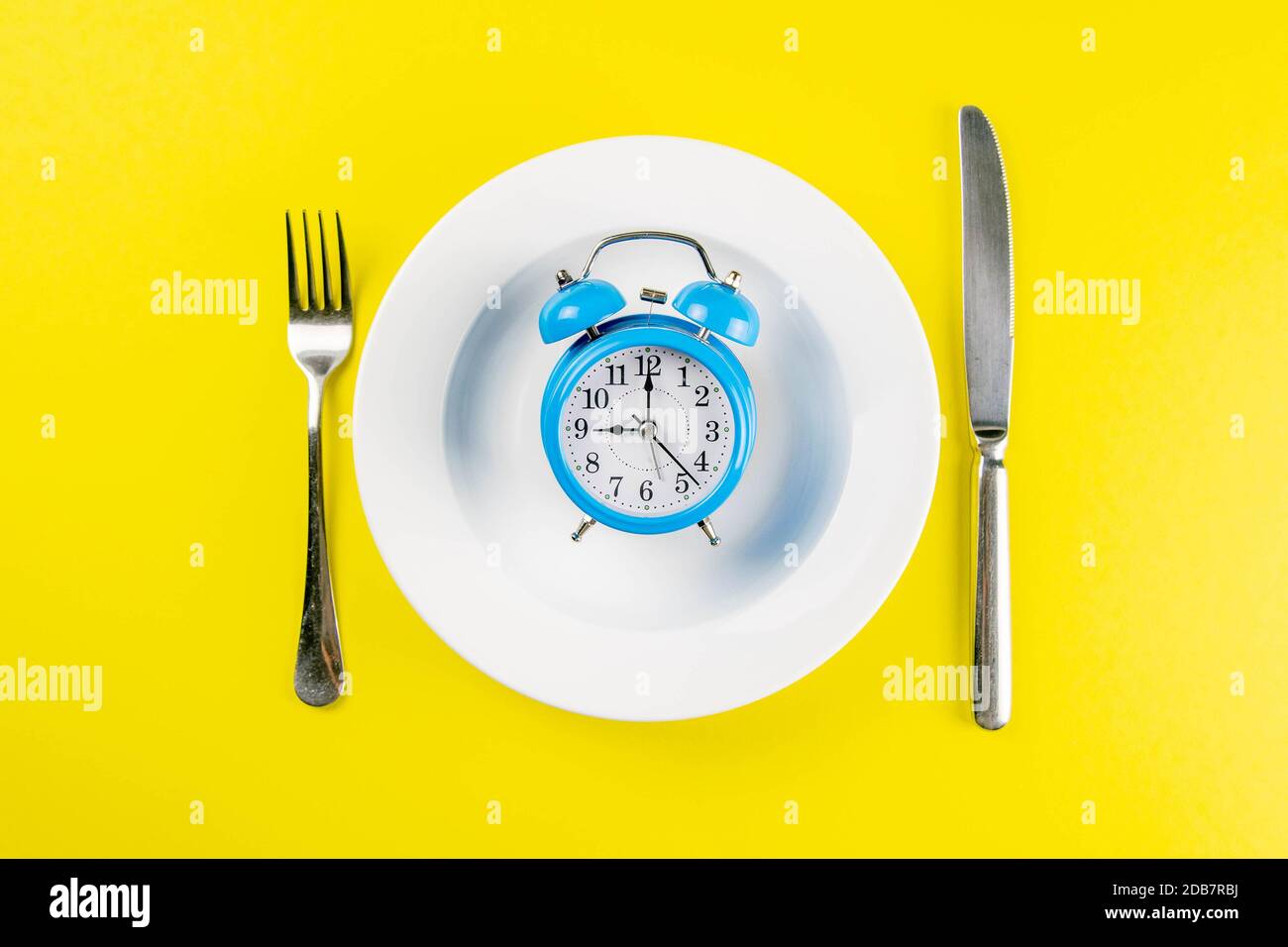 Alarm clock with fork and knife on the blue plate on blue table. Time ...