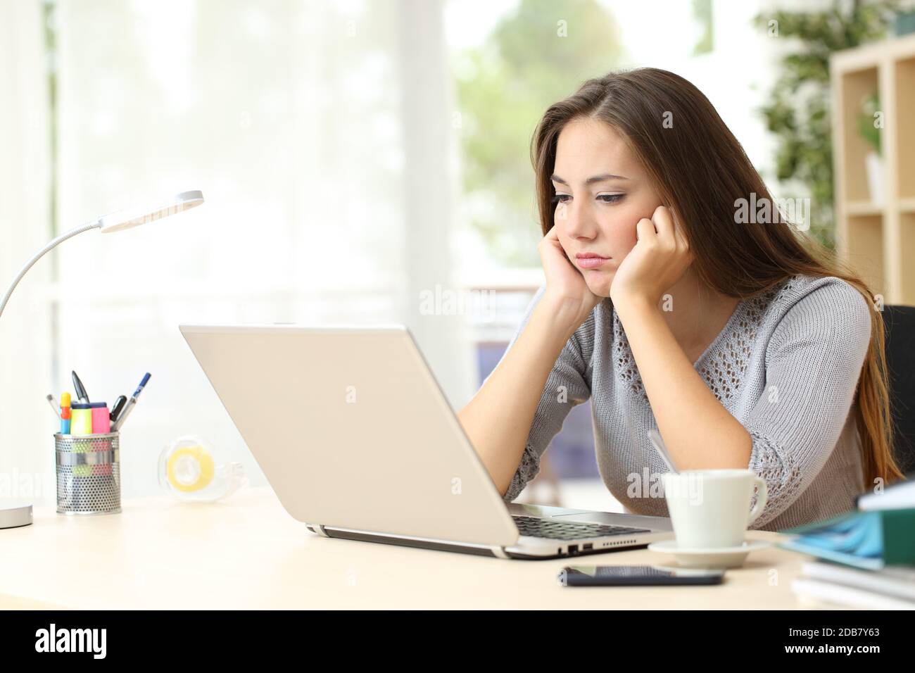 Bored entrepreneur woman looking at laptop screen sitting on a desk at ...