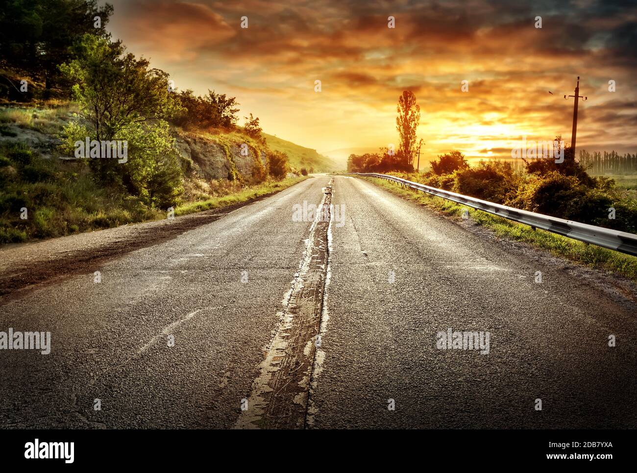 Asphalt road receding into the distance under a dramatic sky of fire ...