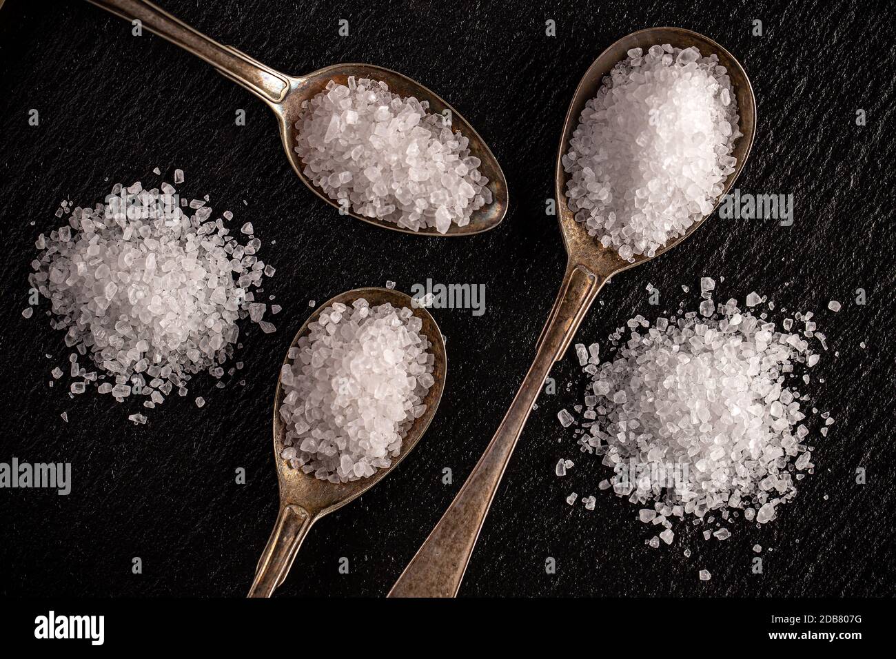 Flat lay of healthy sea salt in vintage spoons on black background ...