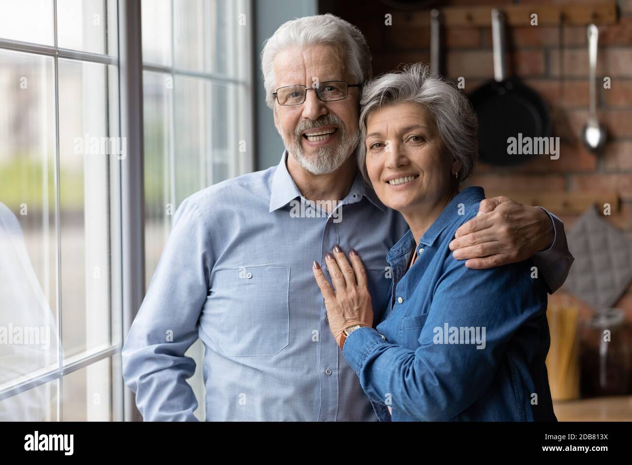 Head shot portrait smiling mature couple hugging, standing in kitchen ...