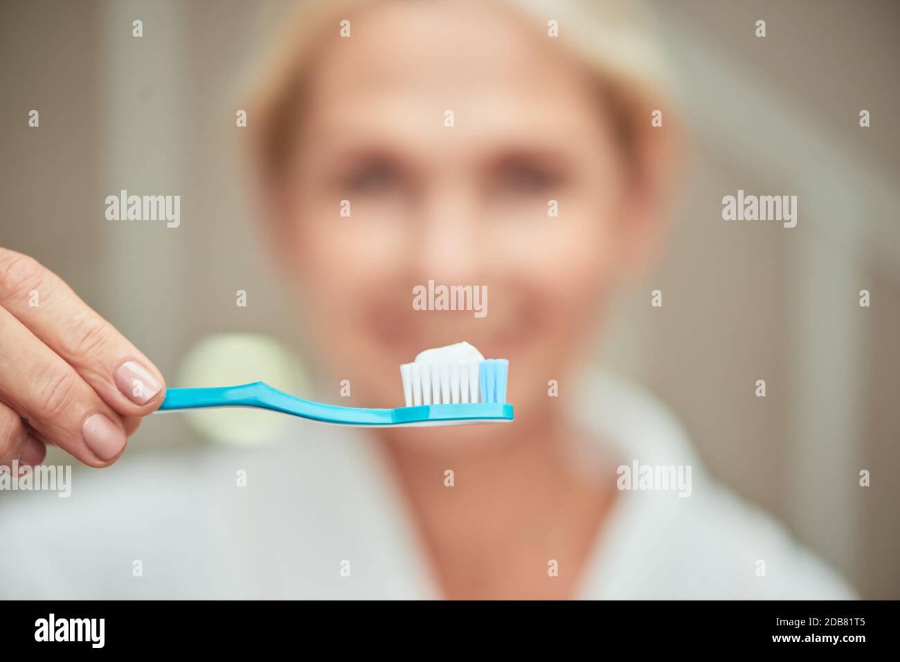 Toothbrush with white paste in hand on blurred woman in spa background ...