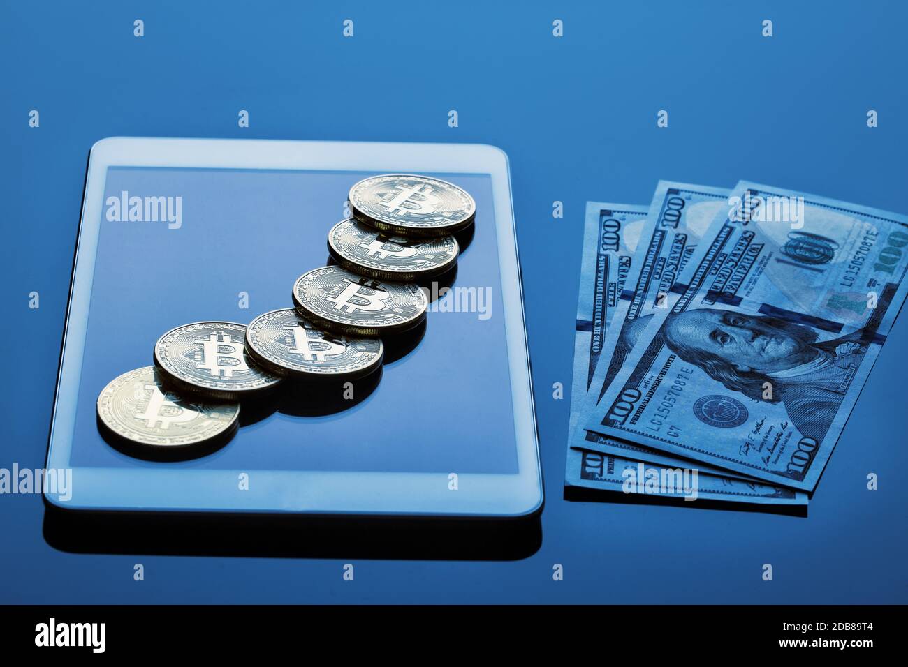 Coins of crypto-currency bitcoin and hundred-dollar bills with a tablet ...