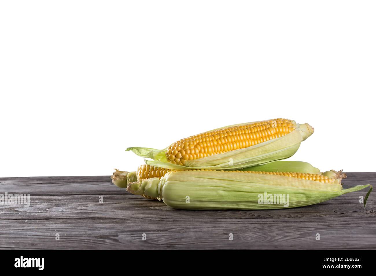 Three cobs of corn with green leaves on wooden table isolated on white ...