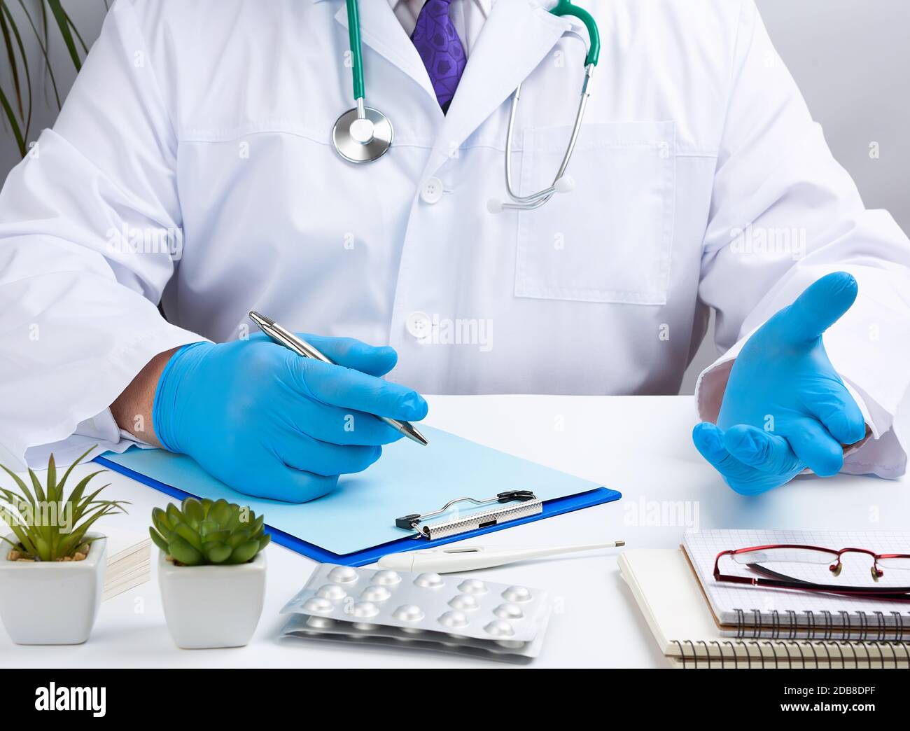 doctor in a white uniform sits at a white table and writes in a paper ...