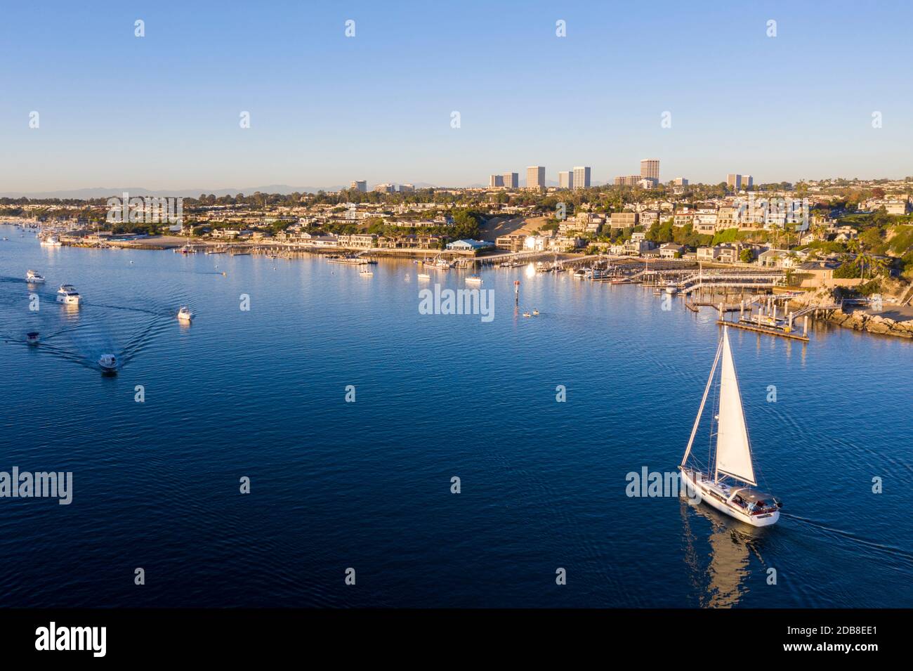 Aerial view above a sailboat entering Newport Harbor with the towers of ...