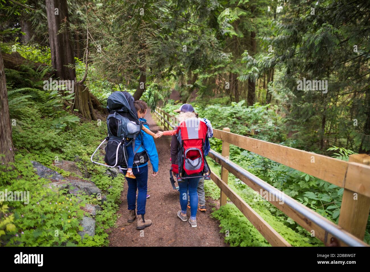 Two toddlers hold hands across the trail while hiking with their moms ...