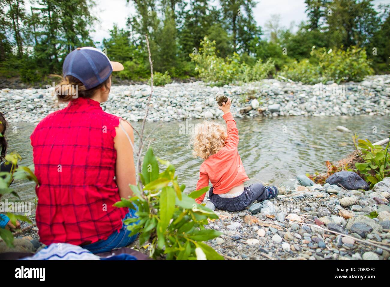 Mother watches her baby throwing a rock into the river Stock Photo - Alamy