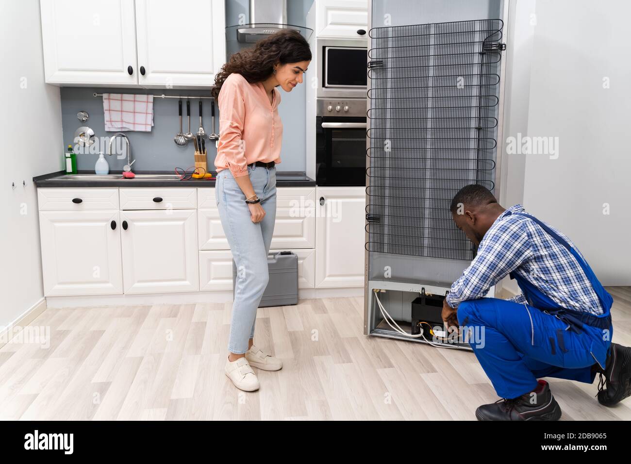 Young Repairman Repairing Refrigerator In Front Of Beautiful Woman ...
