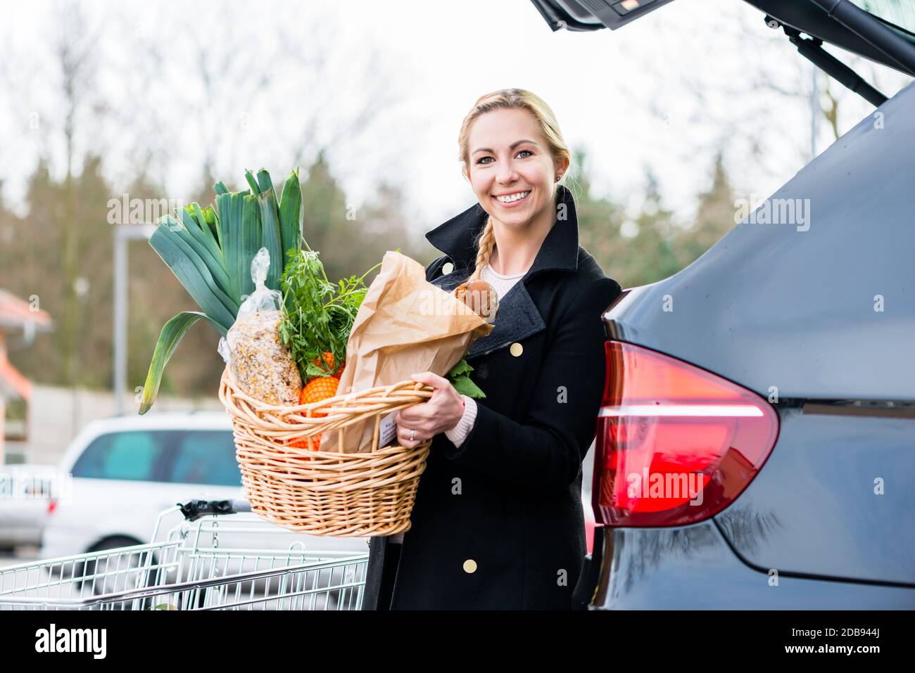 Woman loading groceries after shopping into trunk of her car on parking ...