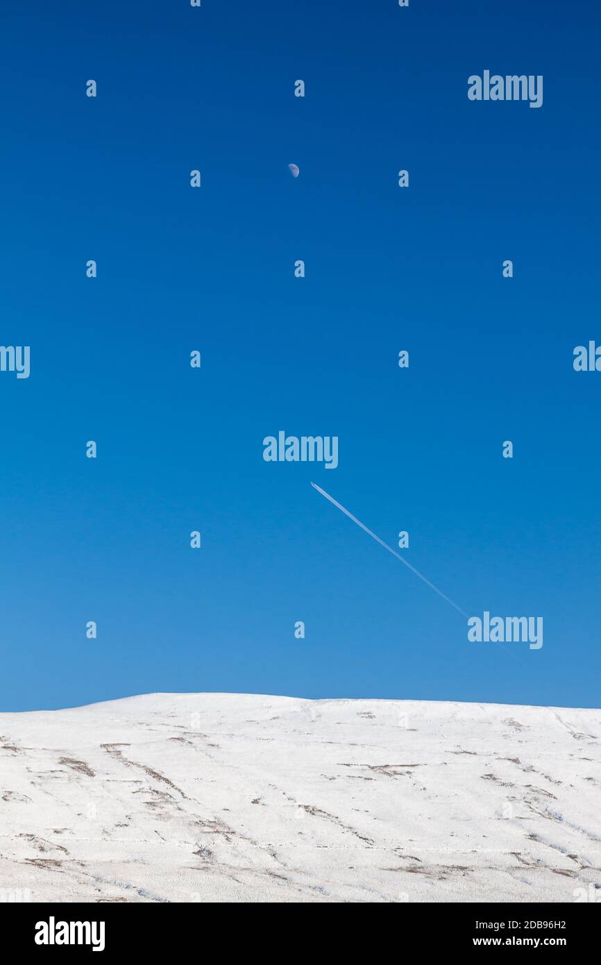 Aircraft contrail in a blue sky over a snow covered mountain scene ...