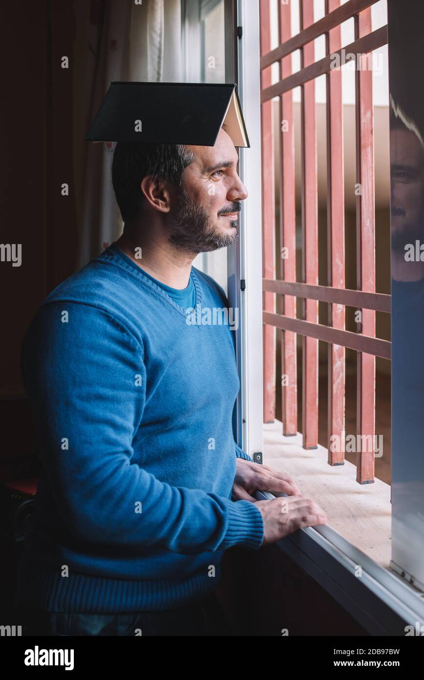 Man leaning out a window with a book on his head Stock Photo - Alamy